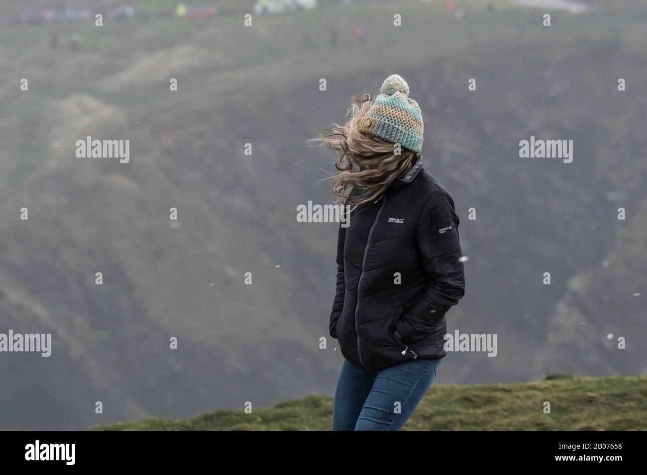 A woman walking in very windy conditions with her hair blowing across ...