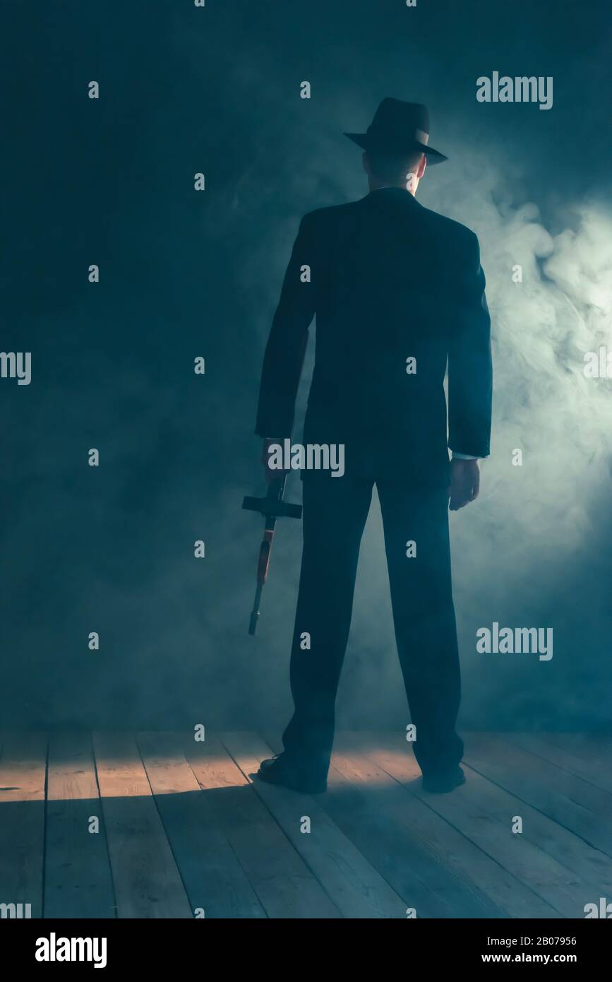 Retro gangster stands with machine gun in smoky room. Rear view Stock ...