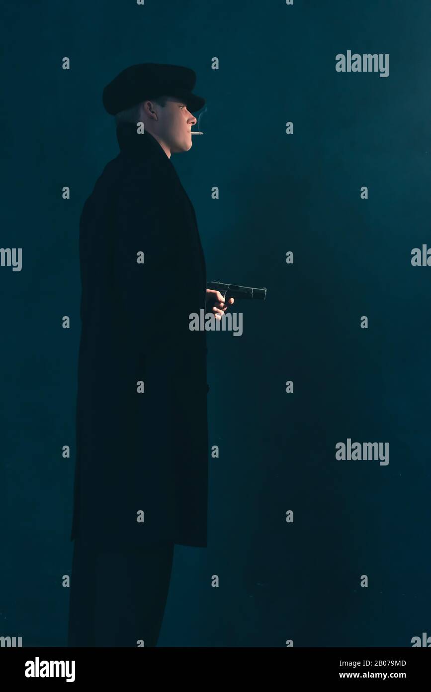 Retro mobster with cigarette shoots with gun. Side view Stock Photo - Alamy