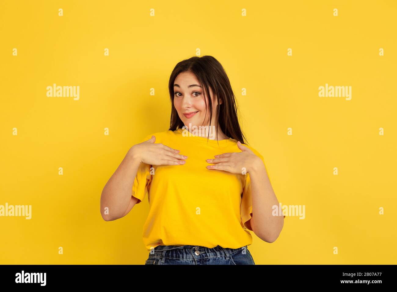Pointing on herself. Caucasian woman's portrait isolated on yellow ...