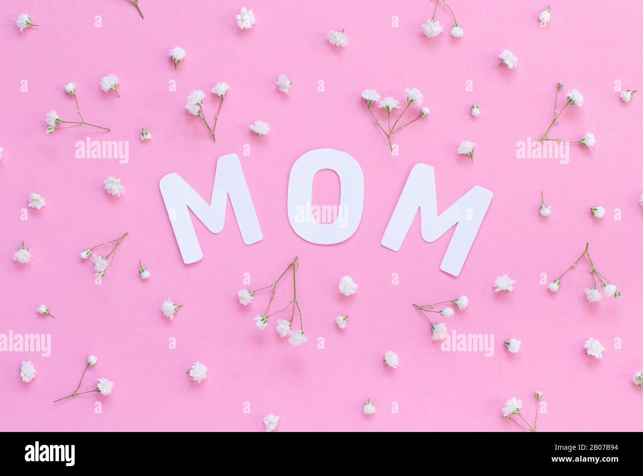 Small white flowers and word MOM on a light pink background top view ...