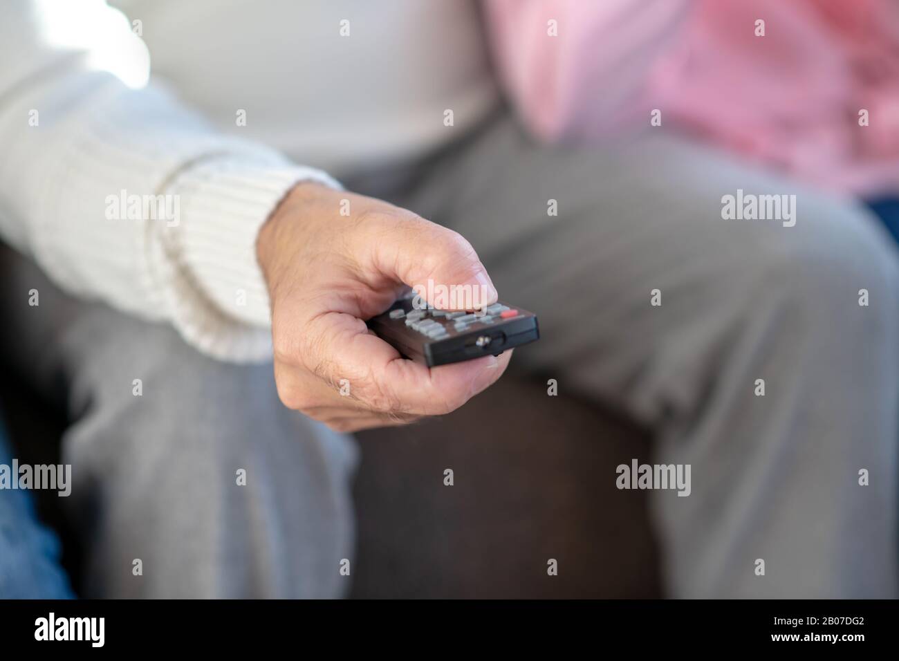 Close up picture of a man sitting on the sofa with a remote control in ...
