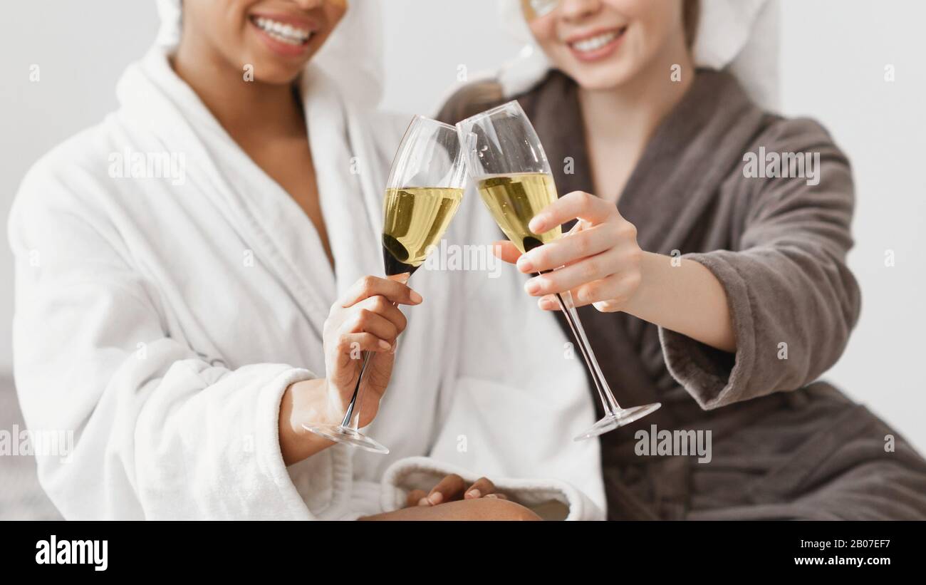 Cropped of two multiethnic ladies cheering with glasses of champagne ...