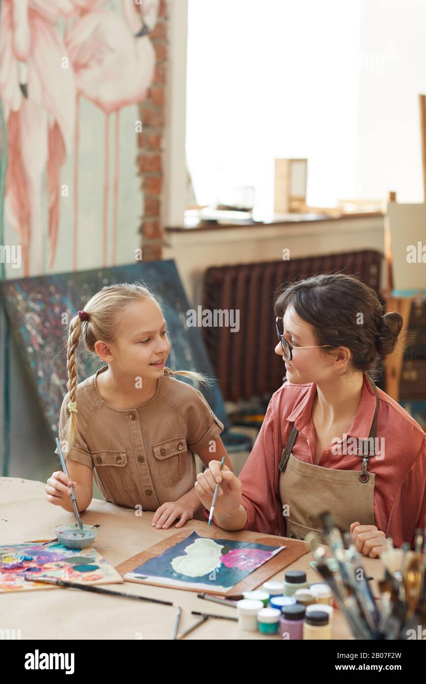 Young woman painting with little girl together at the table and talking ...