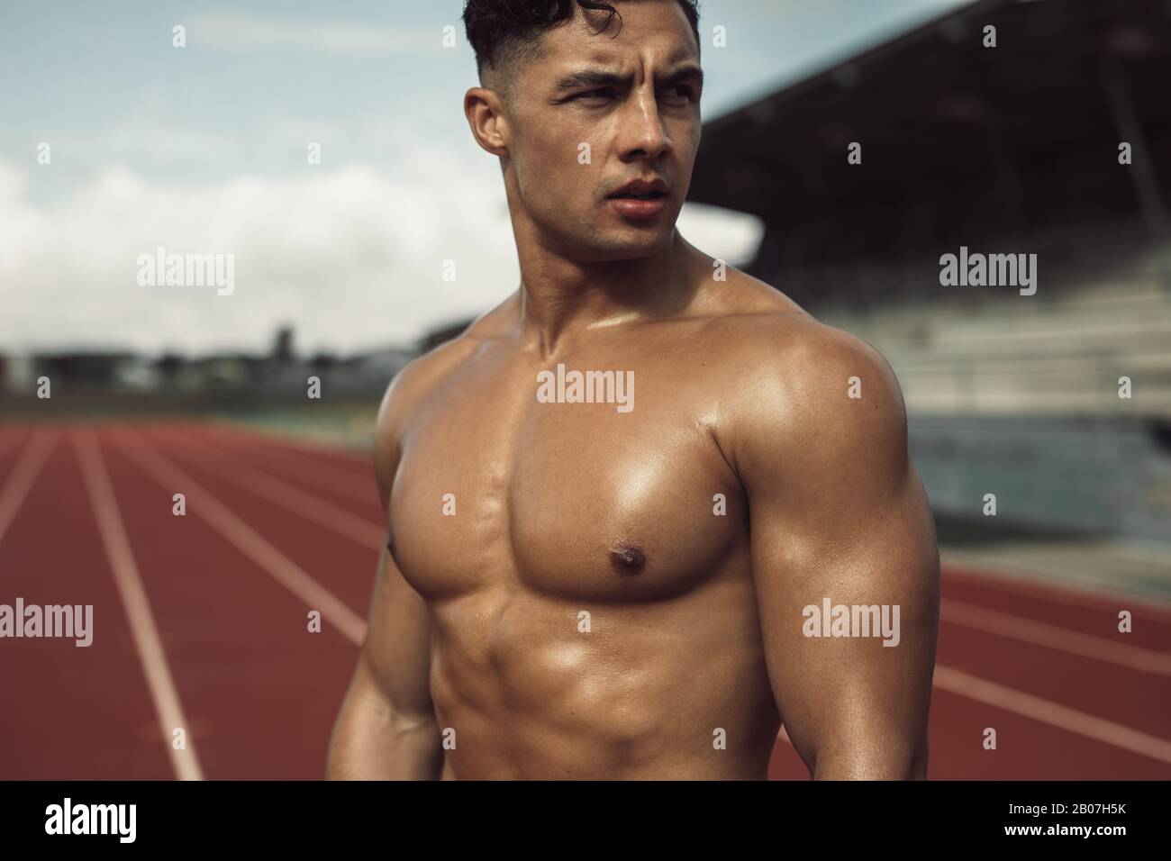 Muscular man standing on track field outdoor while relaxing after ...