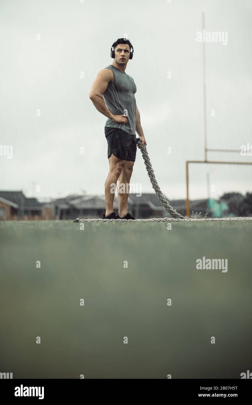 Strong young man standing in the field with a battle rope and looking ...