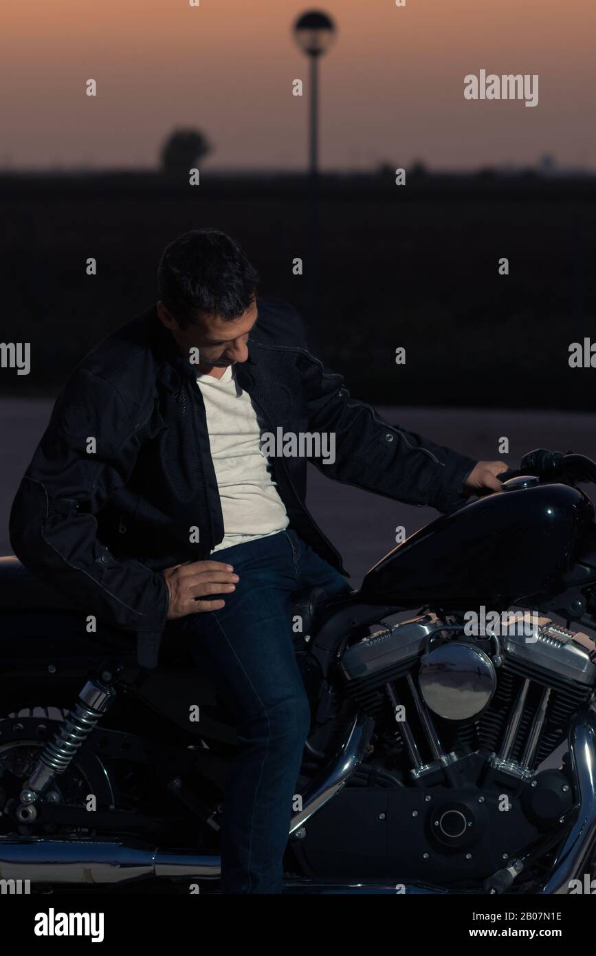 Male biker on his motorcycle looking at the engine Stock Photo - Alamy