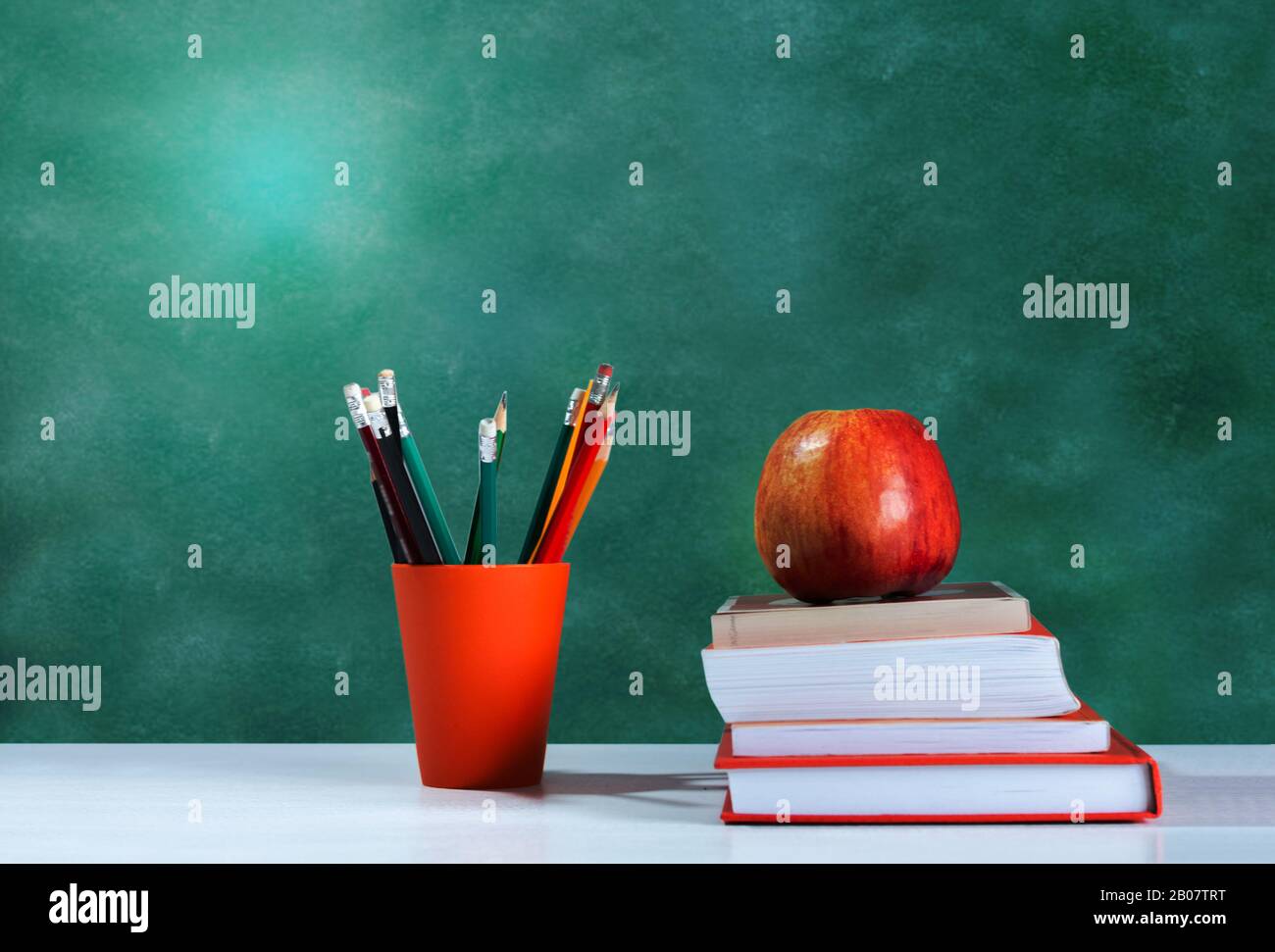 Back to school, orange pencil holder, stack of books on white table ...