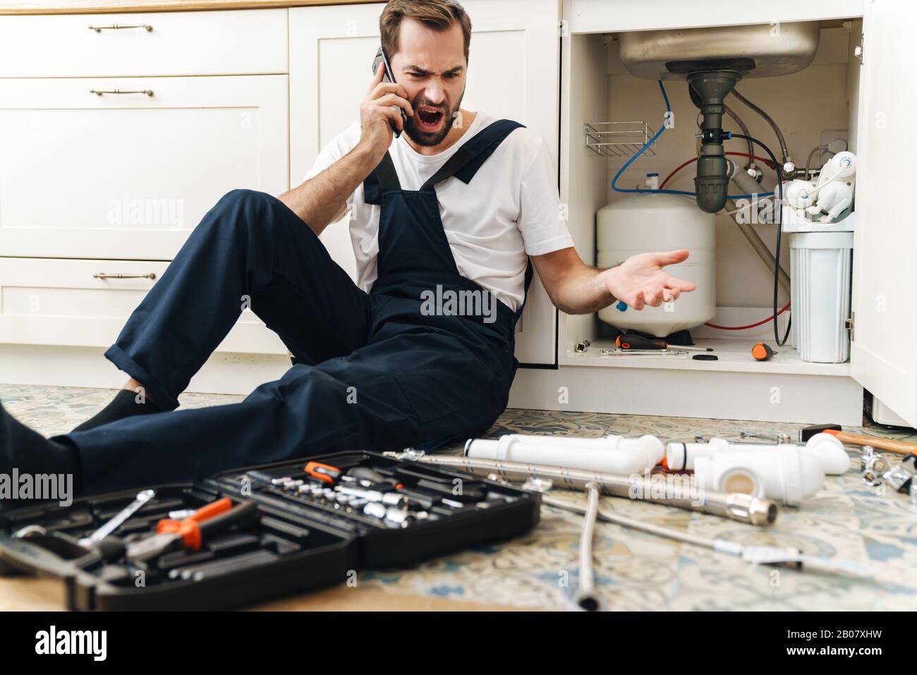 Image of young displeased negative man plumber work in uniform indoors ...