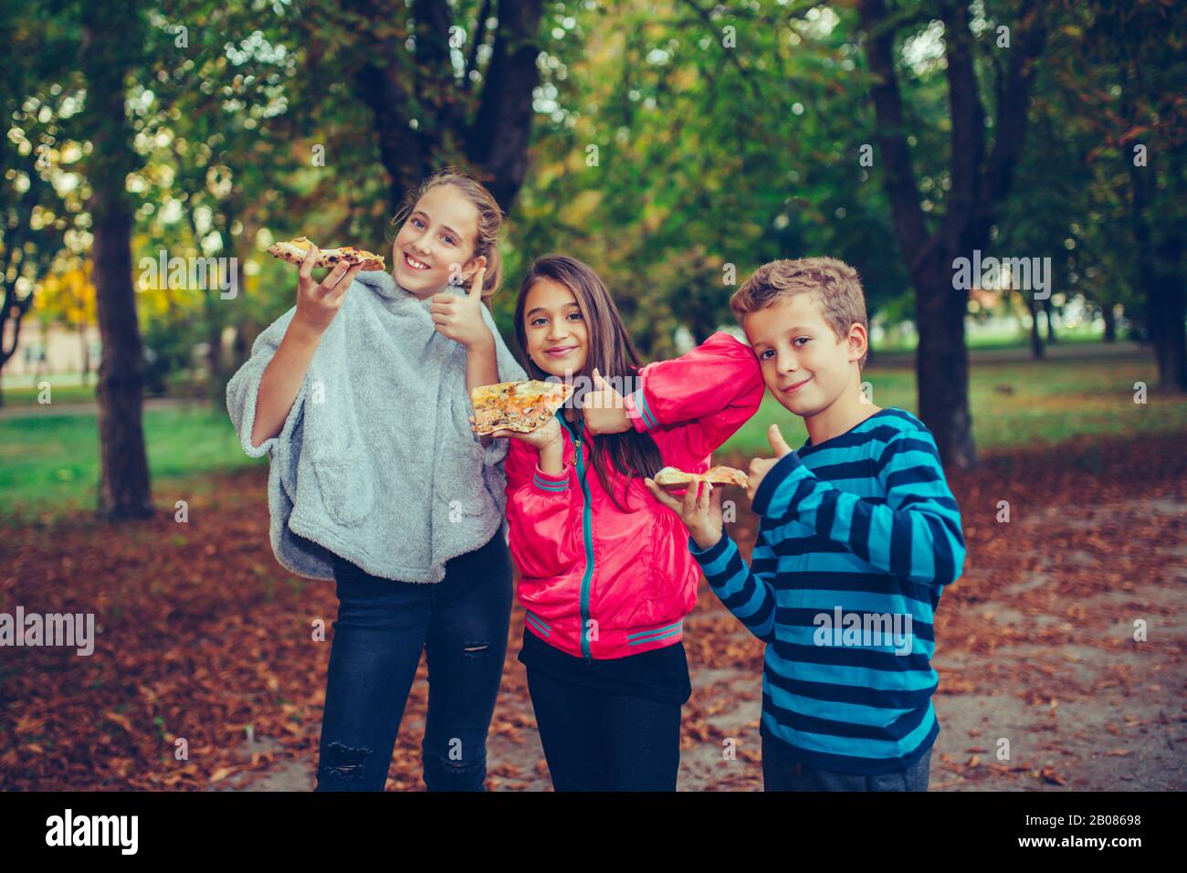 Three happy children talking and eating pizza outdoors, having fun ...