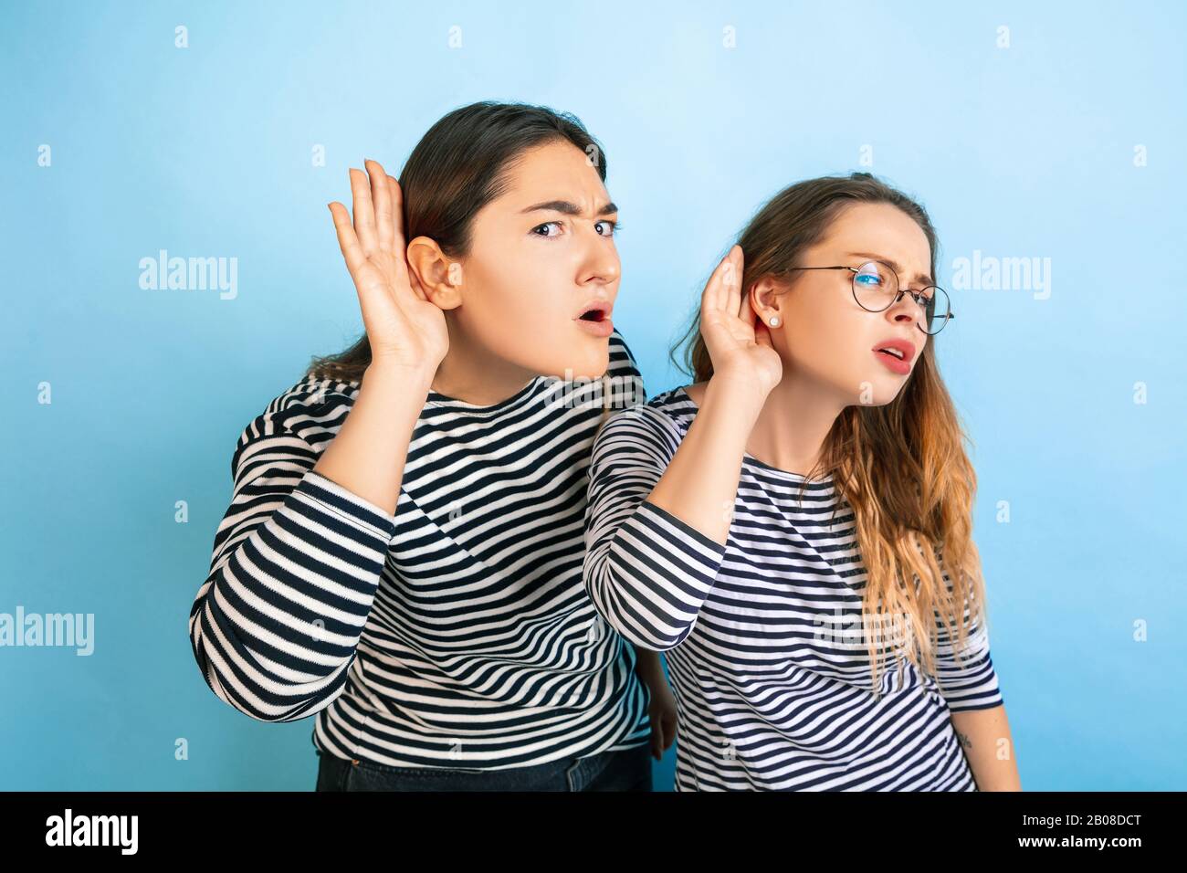 Listen to secrets. Young emotional women isolated on gradient blue ...