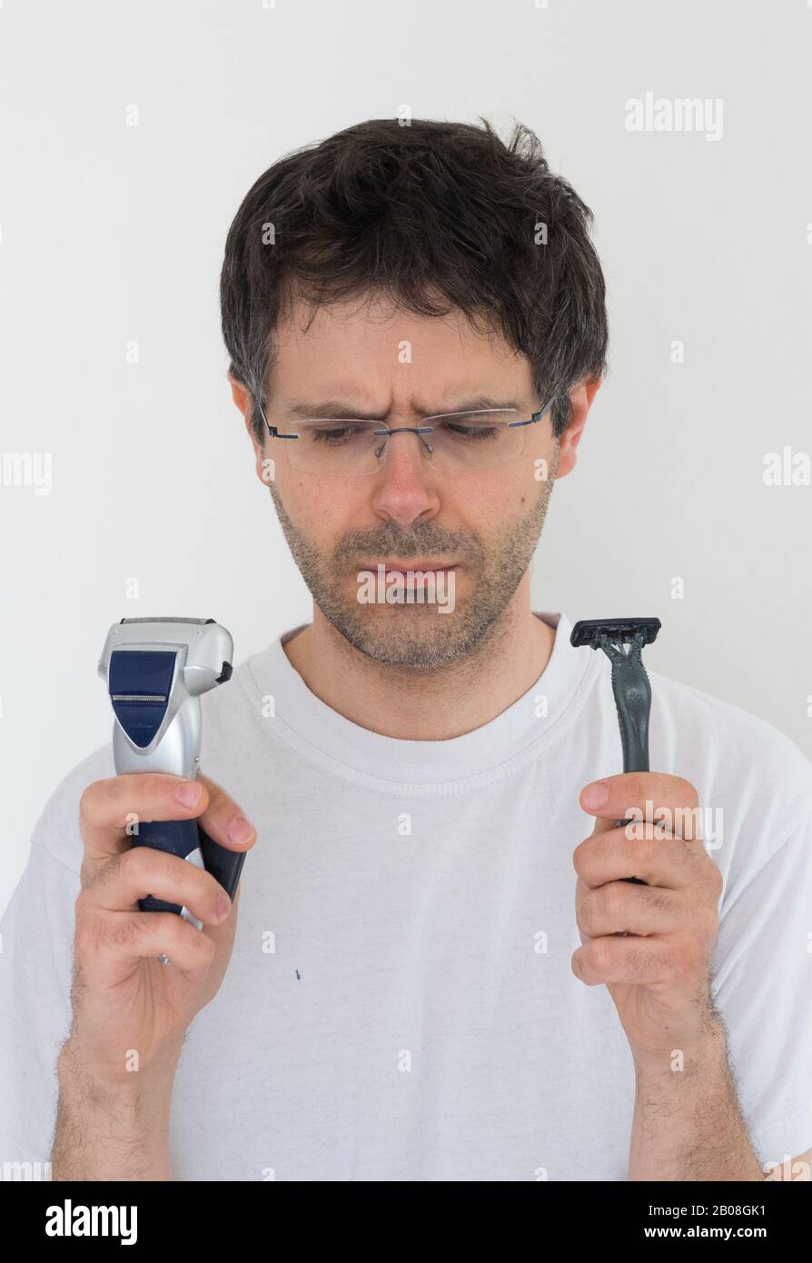 Man with beard undecided whether to use electric razor or razor blade ...