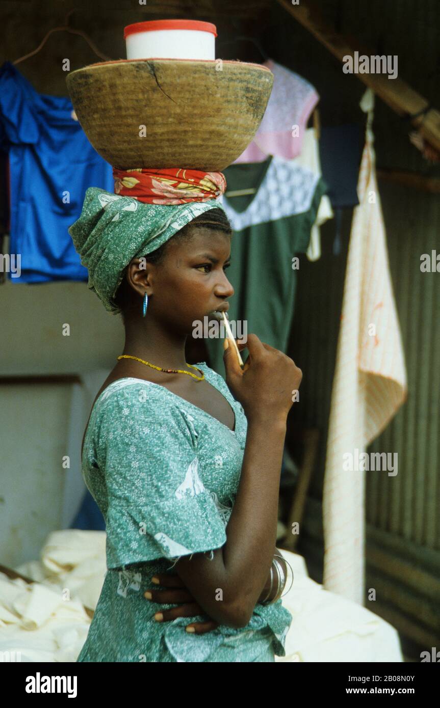 A young woman carrying a basket on her head at an open air market in ...