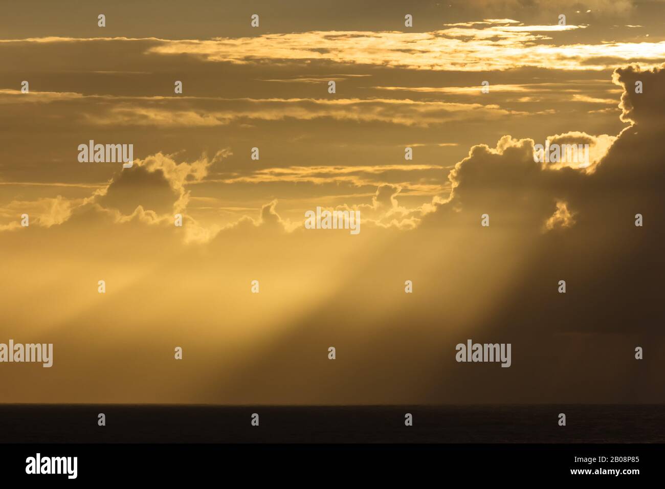 Crepuscular rays of the setting sun hit the clouds hanging above the ...