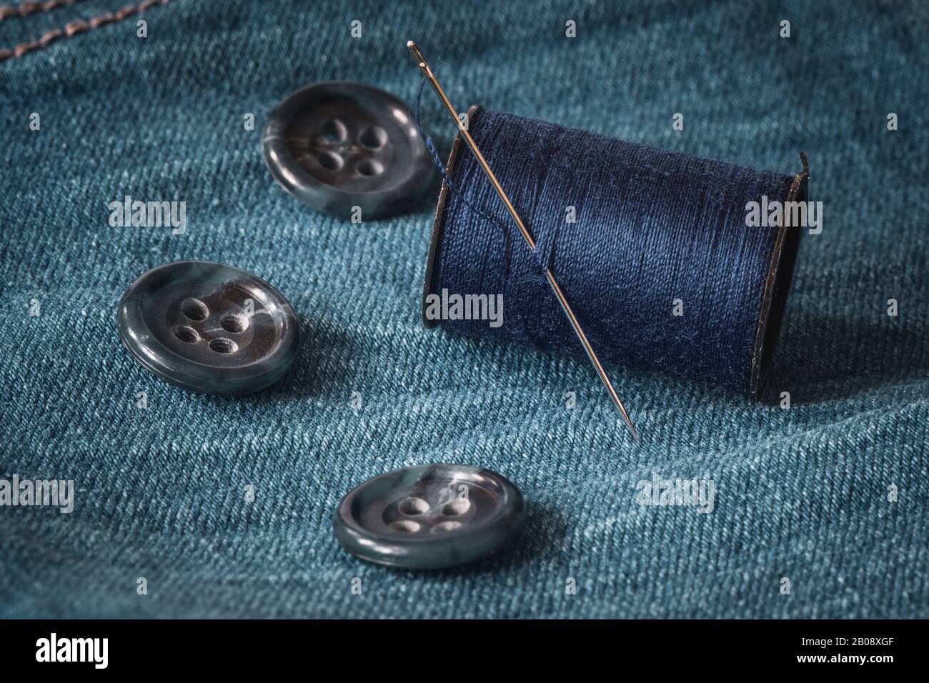 Needle, buttons and spool of thread on jeans fabric Stock Photo - Alamy