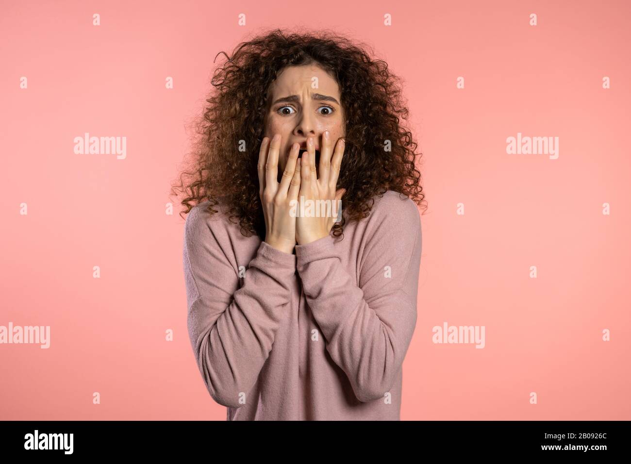 Close up of young scared curly girl shouting isolated over pink ...