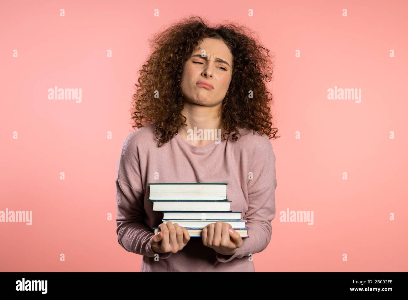 Cute female student is dissatisfied with amount of homework and books ...