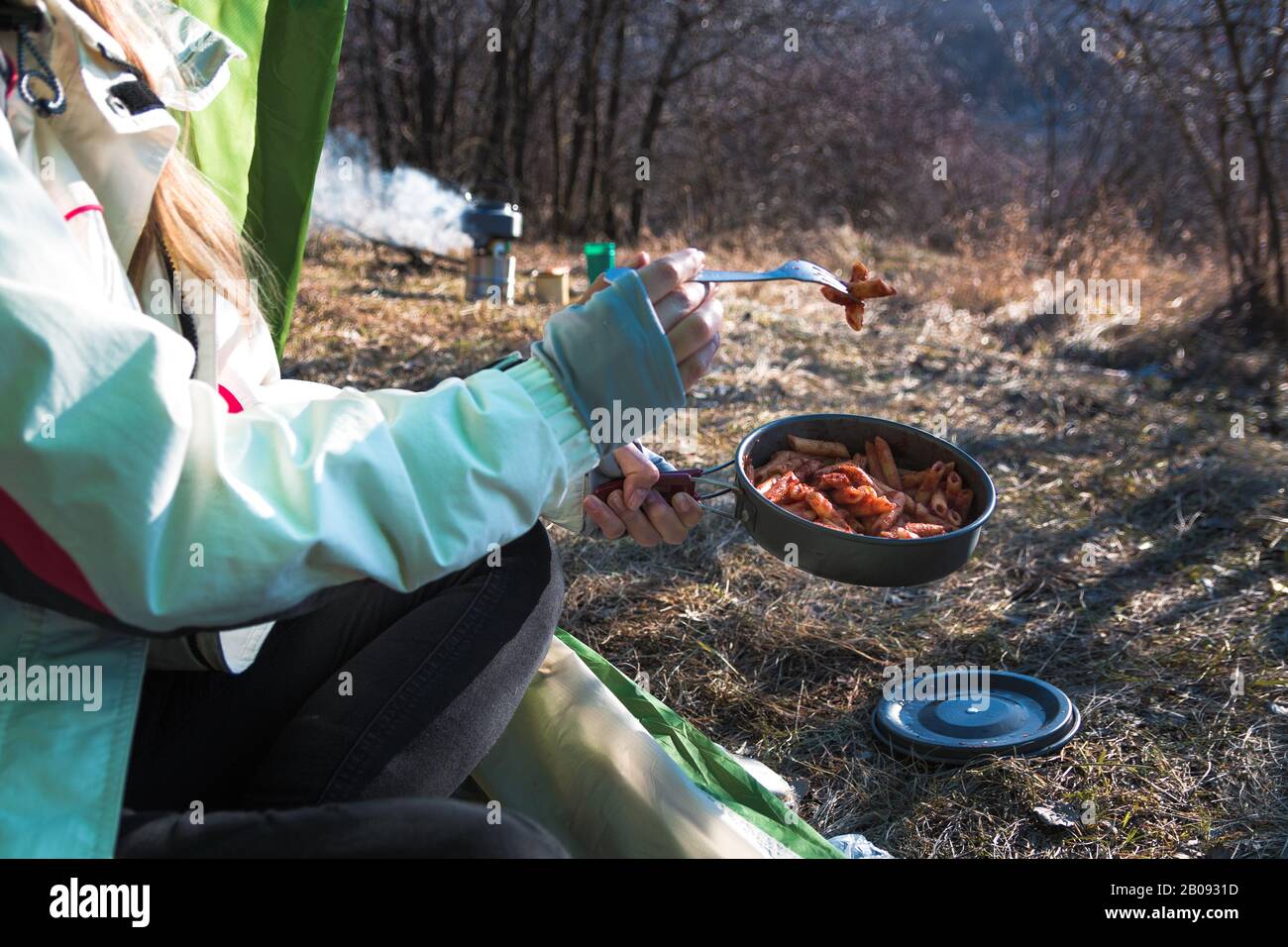 closeup up view of a woman in mountains in tent eating pasta from a pot ...