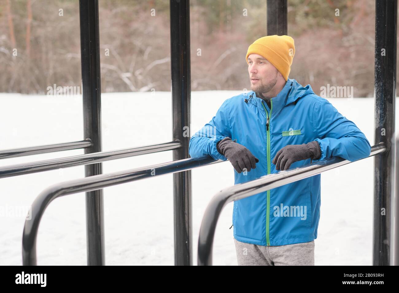 Serious young man with stubble standing between parallel bars on sports ...