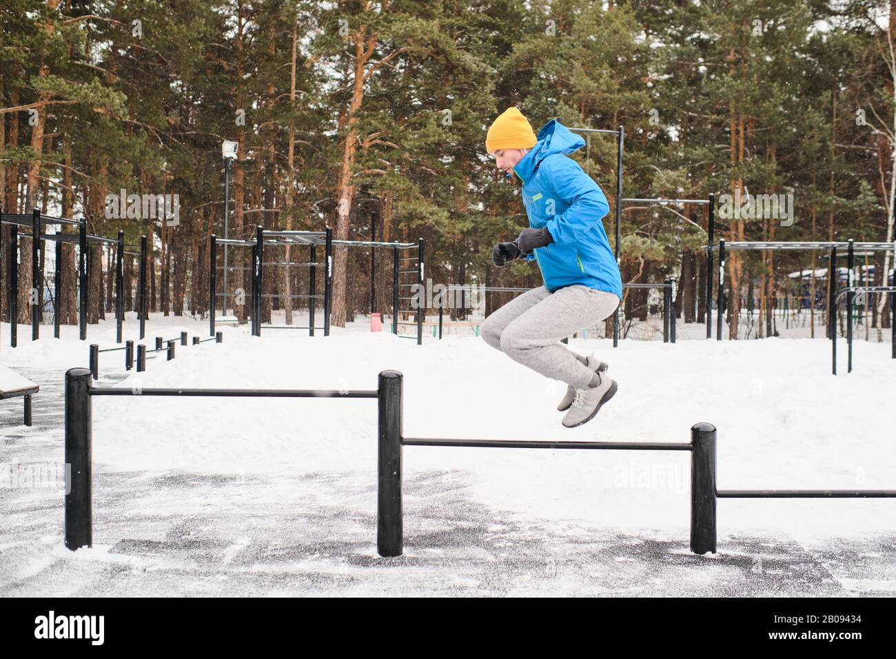 Side view of young man in blue jacket training using horizontal bars as ...
