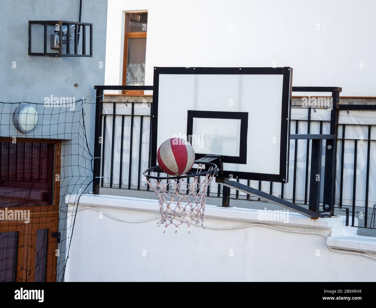 The ball flies into a basketball net attached to white wall in the yard ...