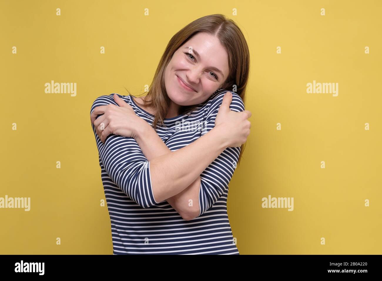 Relaxed happy young woman hugging herself, having pleased joyful facial ...