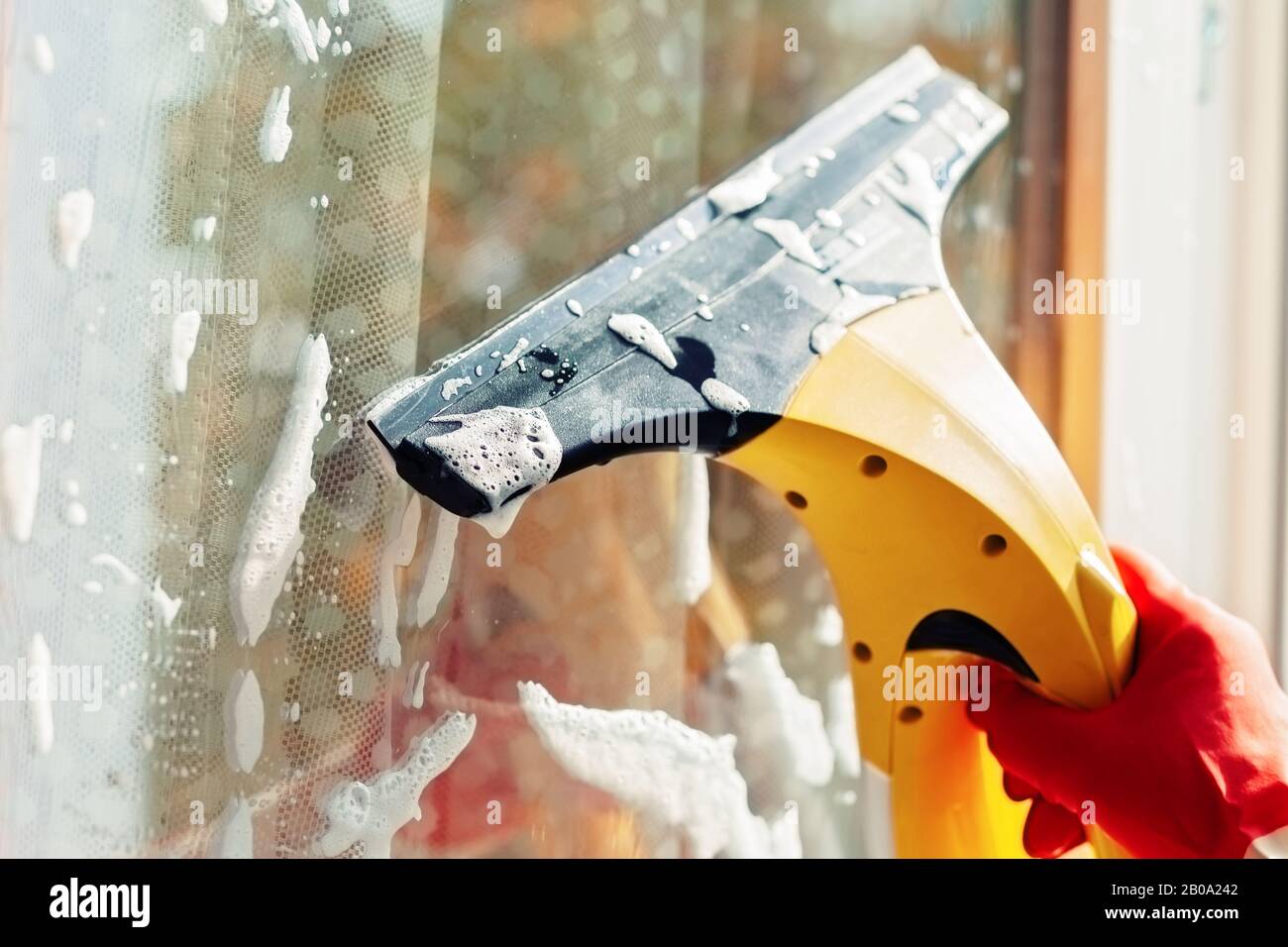 A woman's hand with a rubber glove washes the window with a hand wiper ...