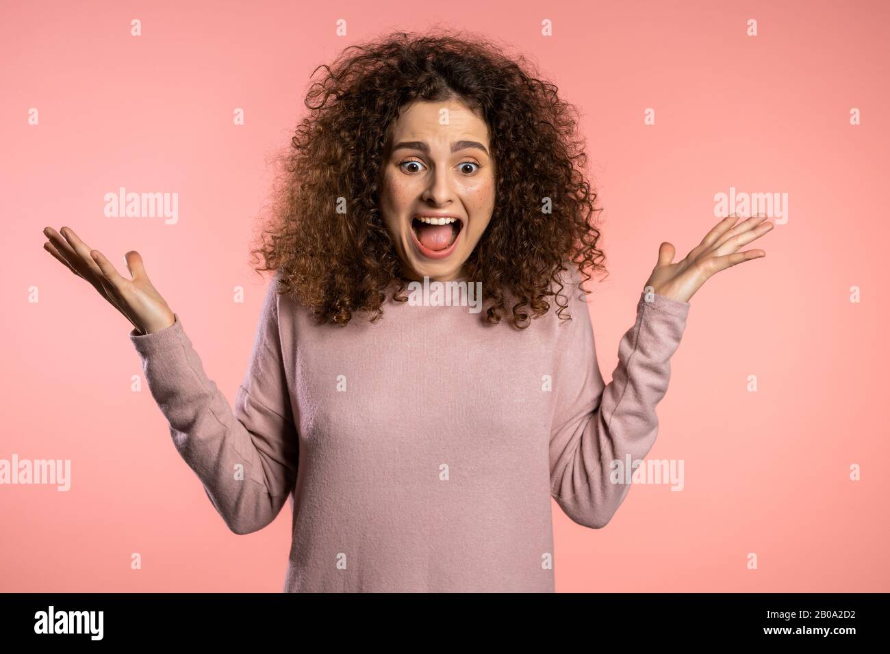 Close up of young scared curly girl shouting isolated over pink ...