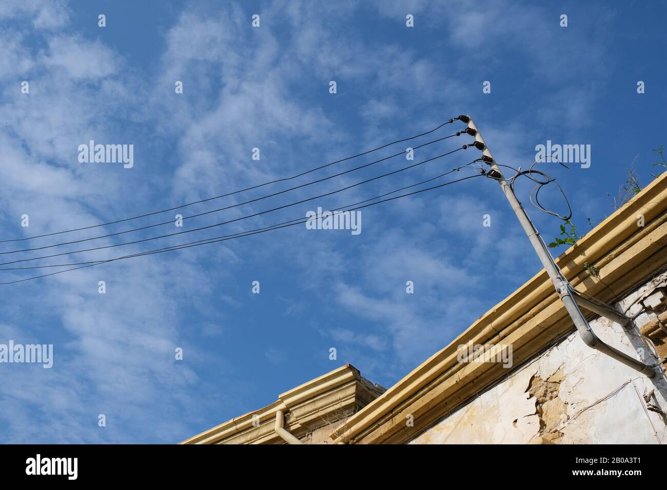 Metal electricity pole and electric wires on top of house roof against ...