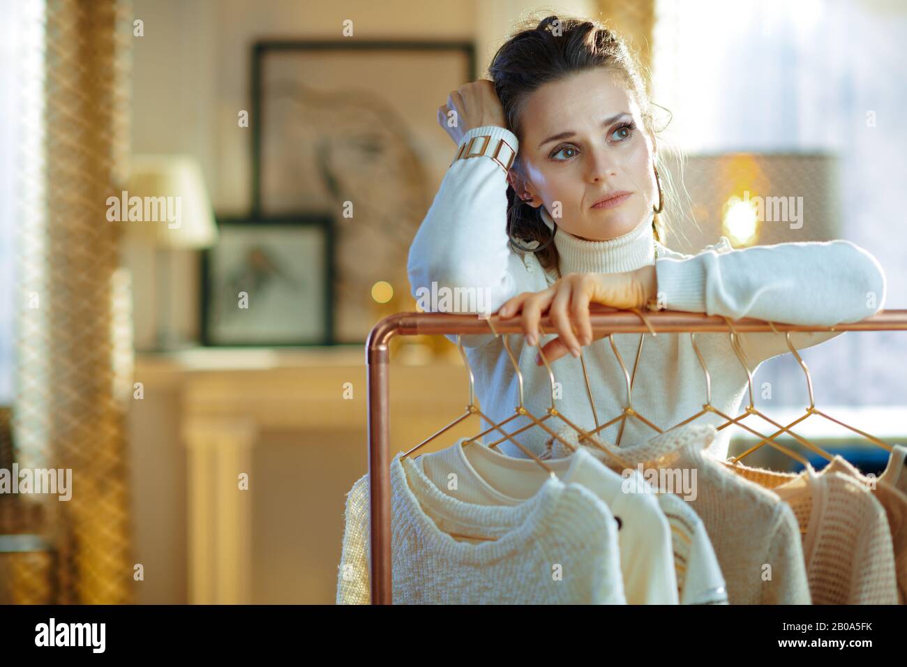 pensive elegant woman in white sweater and skirt near copper clothes ...