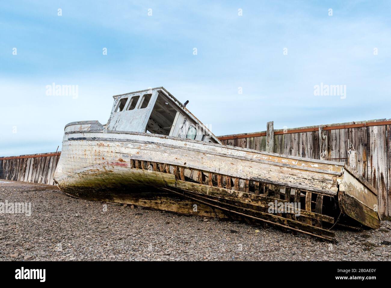 A wrecked boat on the shore next to an old wharf. The boat is in very ...