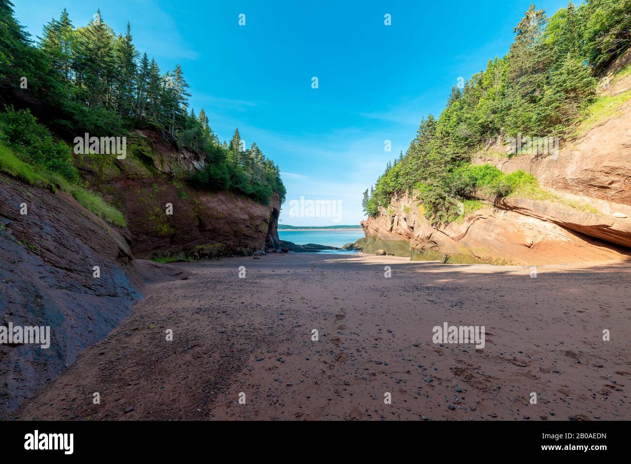 A beach between two cliffs at the ocean. One cliff is in bright ...