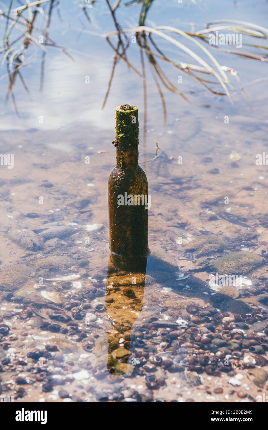 Empty dirty glass bottle in the clear water of the river. Concept of ...