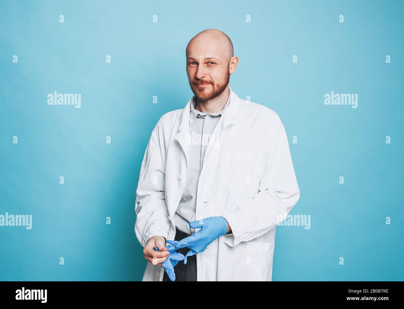 Attractive smiling man bald bearded doctor puts on rubber medical ...