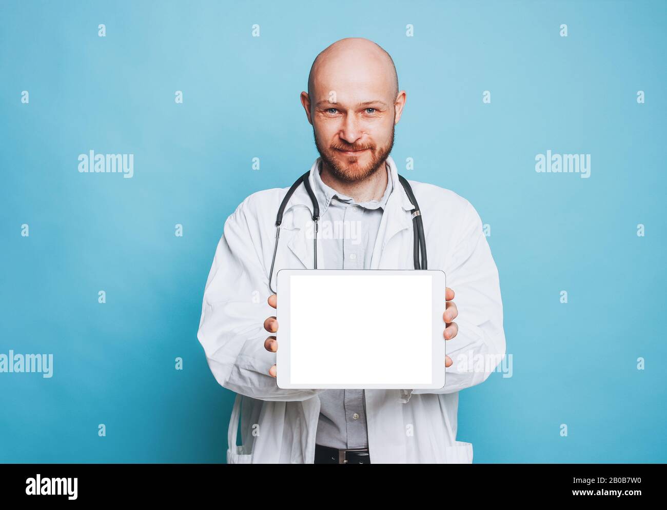 Attractive friendly bald bearded smiling doctor holds tablet with white ...