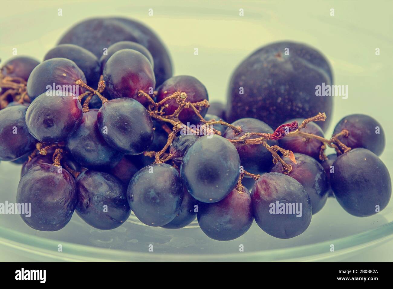 Old and wrinkled purple grapes and plums in a glass bowl Stock Photo ...