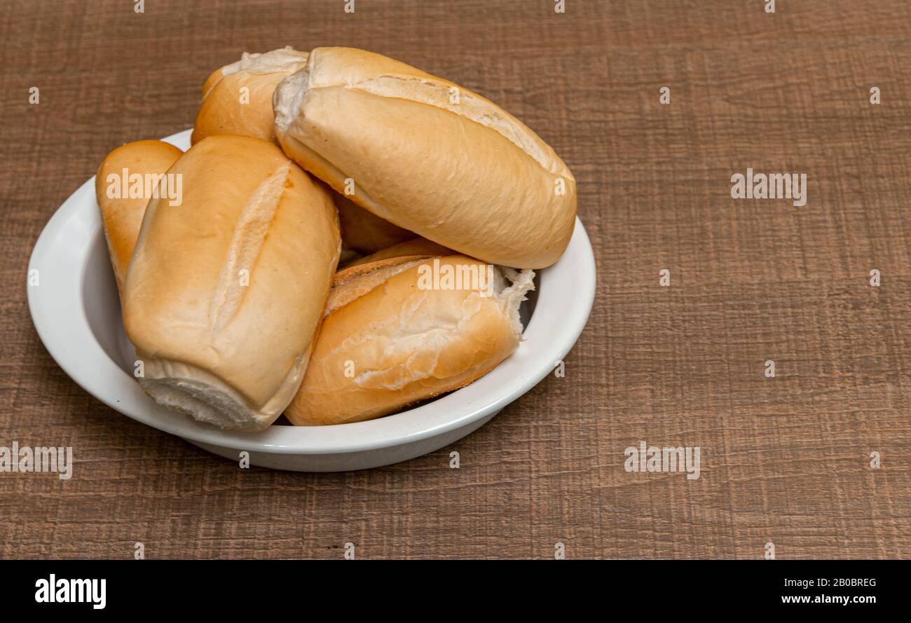 A small bowl with freshly baked wheat breads placed on a wooden table ...