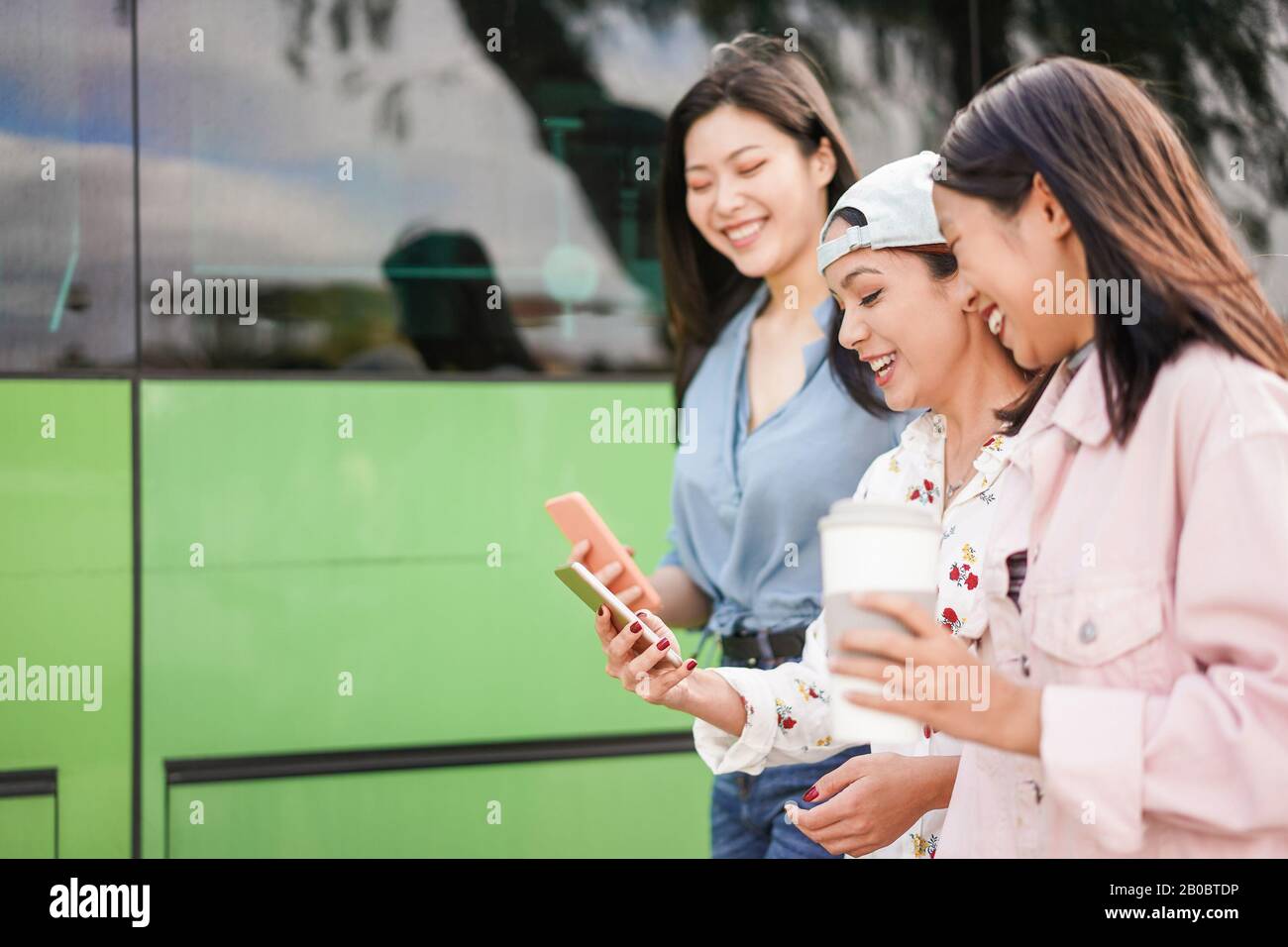 Happy asian friends using smartphones at bus station - Young students ...
