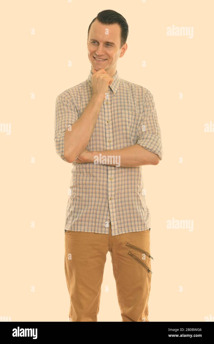 Studio shot of young happy man smiling and standing while thinking ...