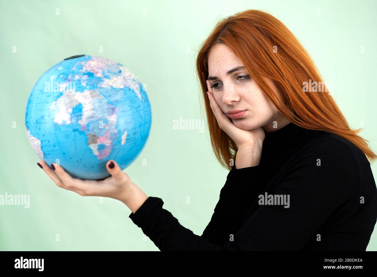Portrait of a sad worried young woman holding geographic globe of the ...