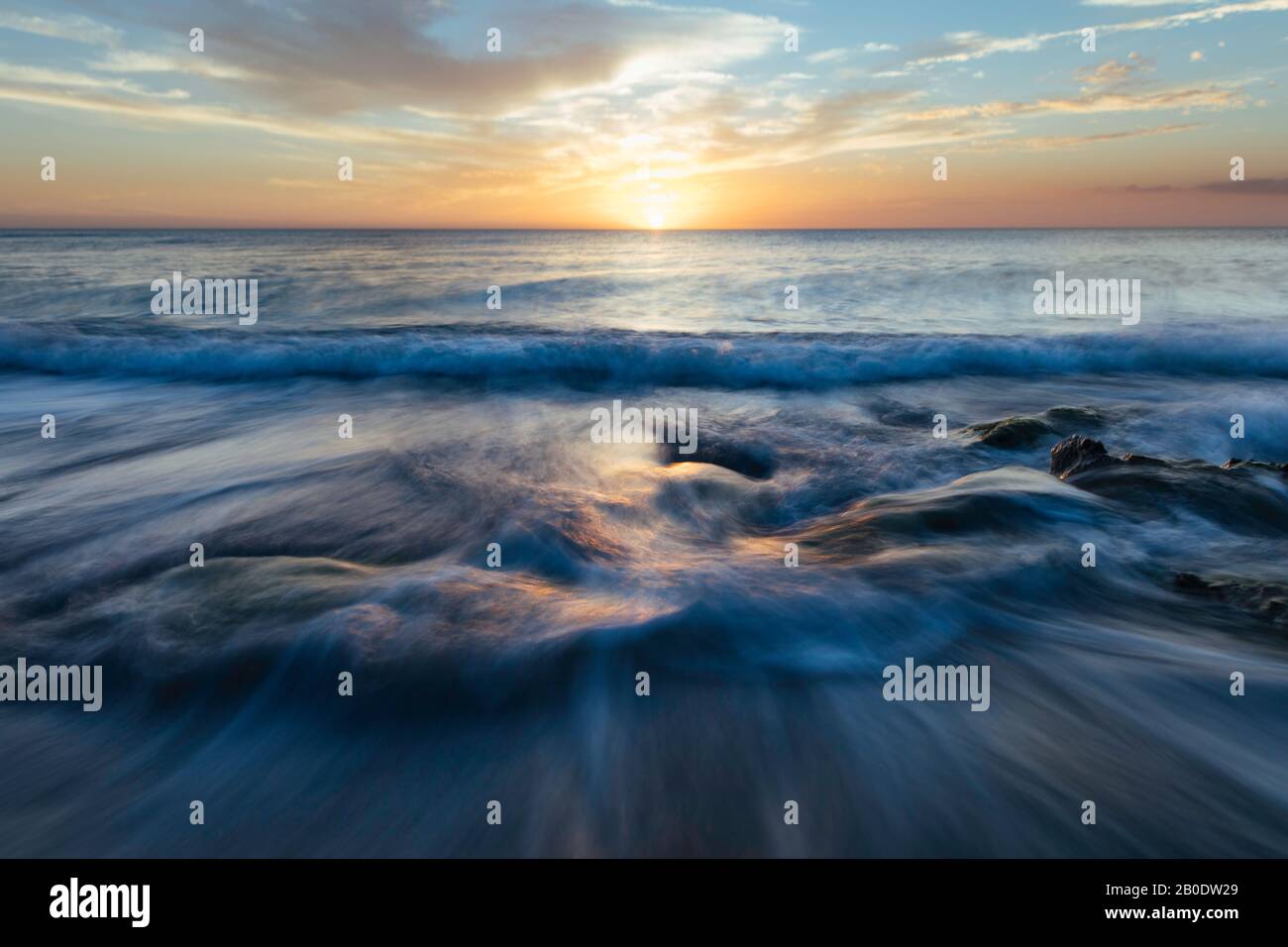 Water flows over rocks at sunset on the beach Stock Photo - Alamy