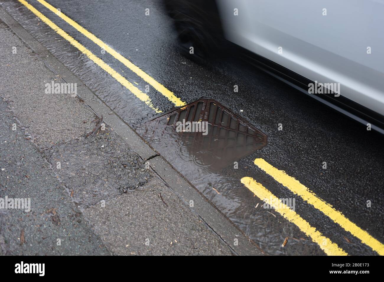 A blocked roadside drainage grid overflowing with rainwater in ...