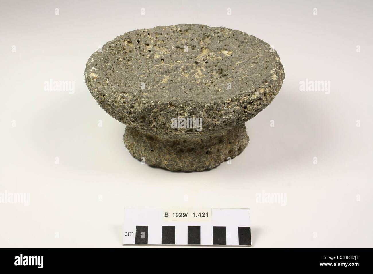 A shallow mortar or bowl made of porous basalt. The object has a foot ...
