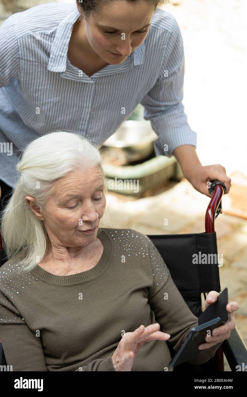 Senior female patient showing mobile phone to young home carer Stock ...