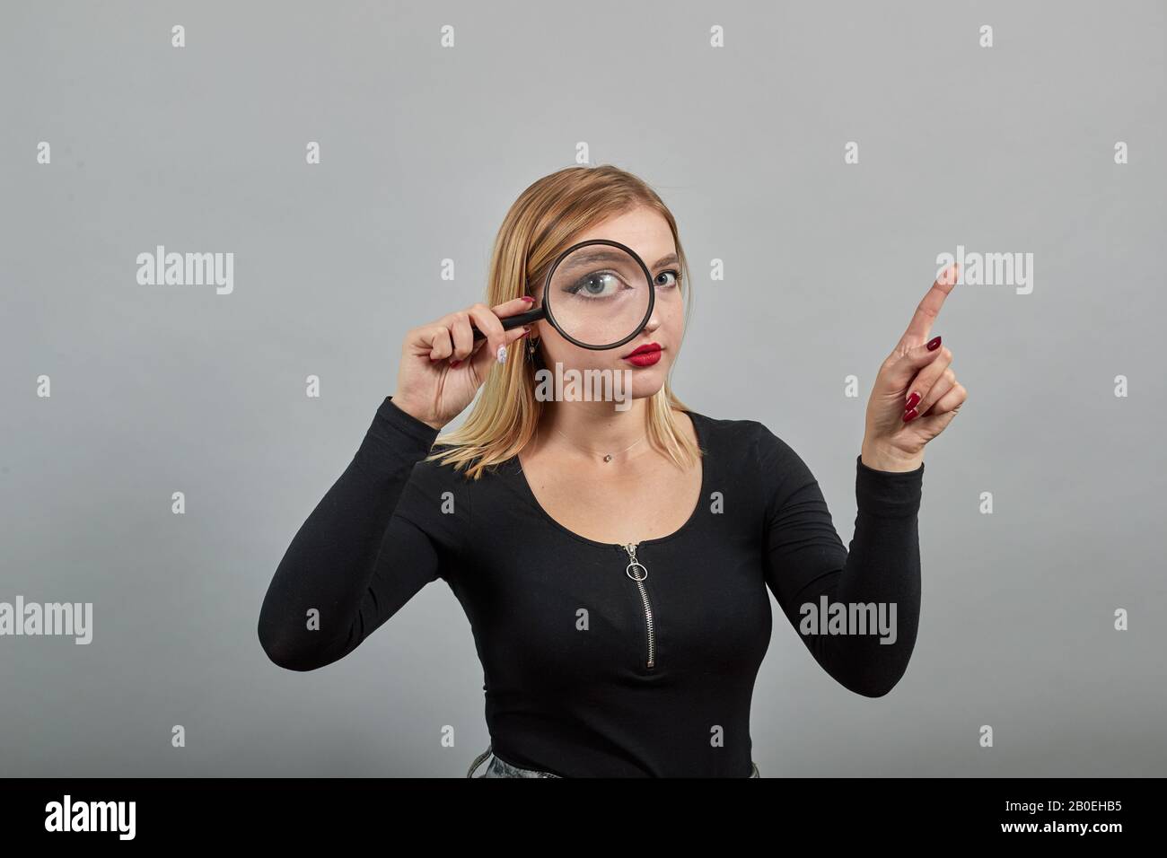 funny woman with magnifier in hand shows eye through magnifying glass ...
