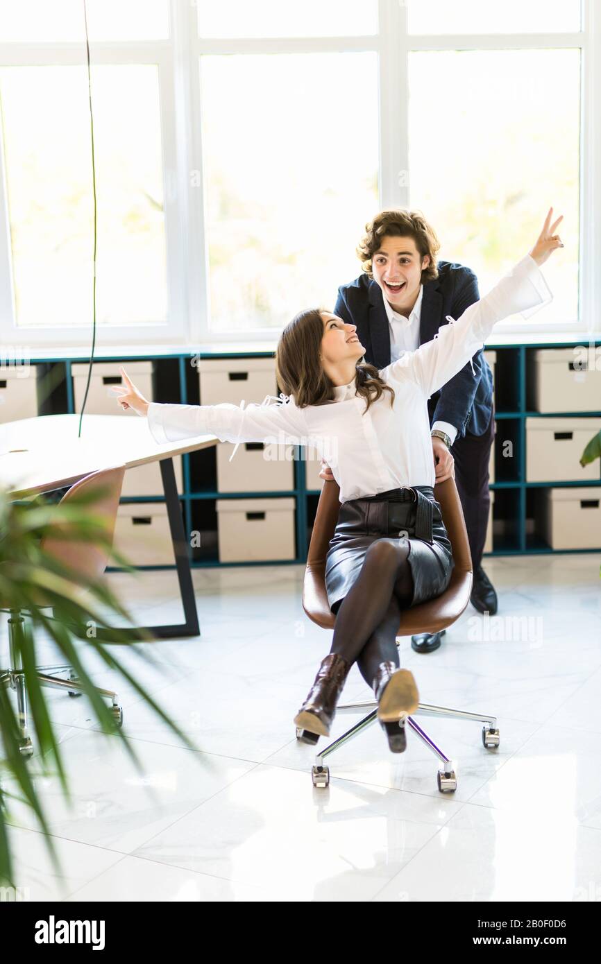 Businesswoman pushing playful colleague in office chair Stock Photo - Alamy