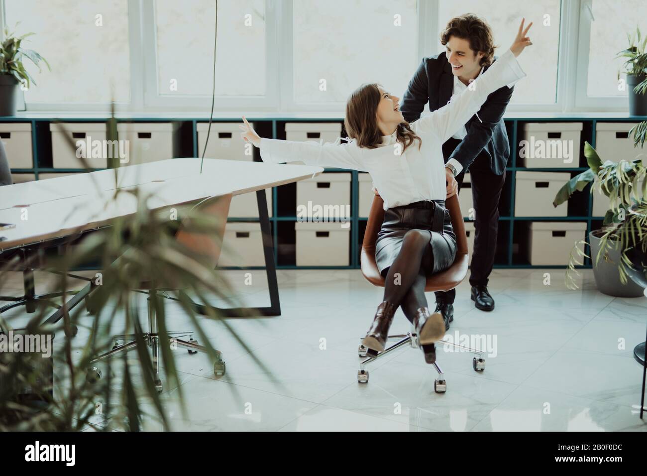 Businesswoman pushing playful colleague in office chair Stock Photo - Alamy