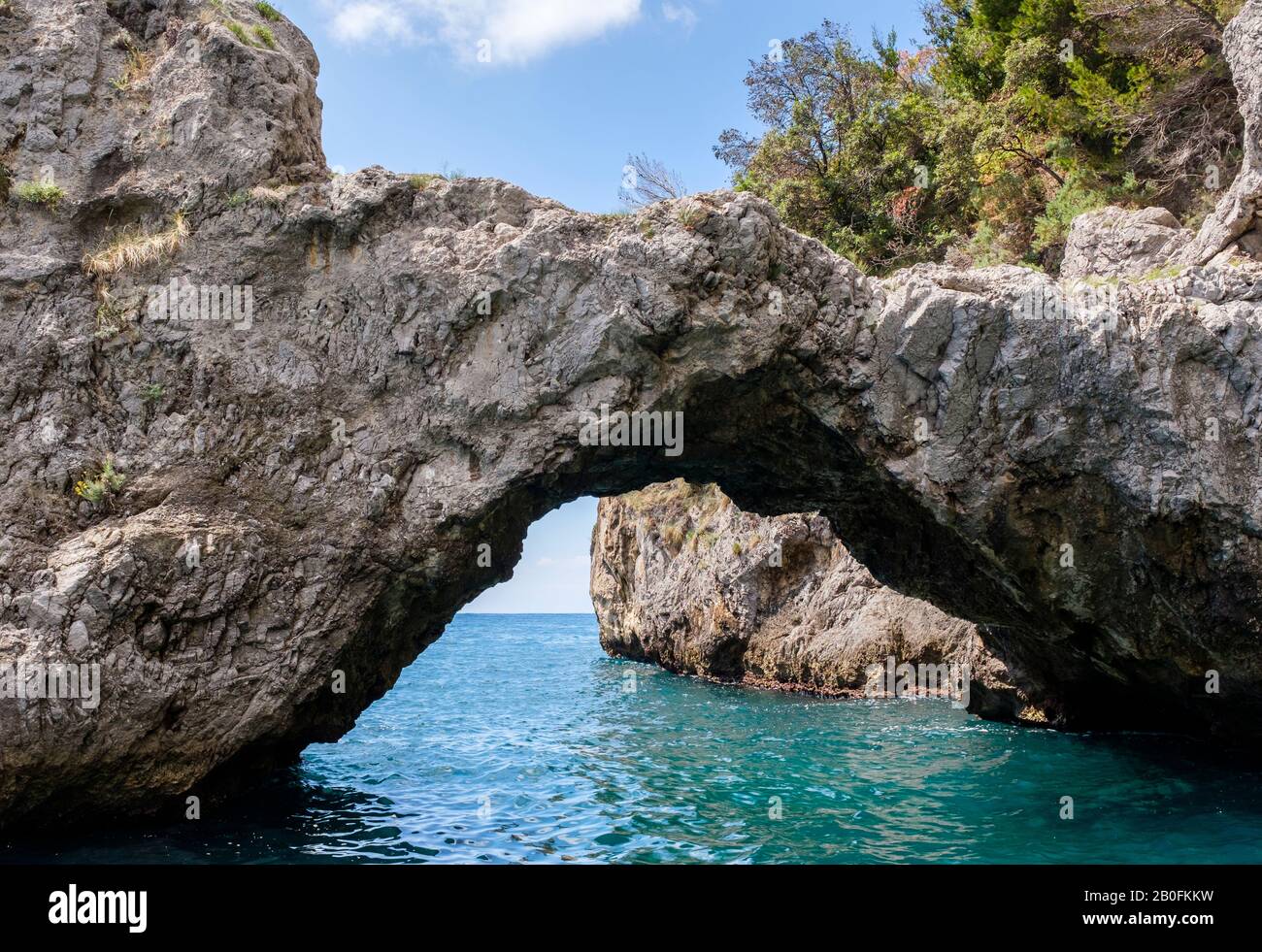 A rocky arch carved by the sea over aqua blue water, along the cliffs ...