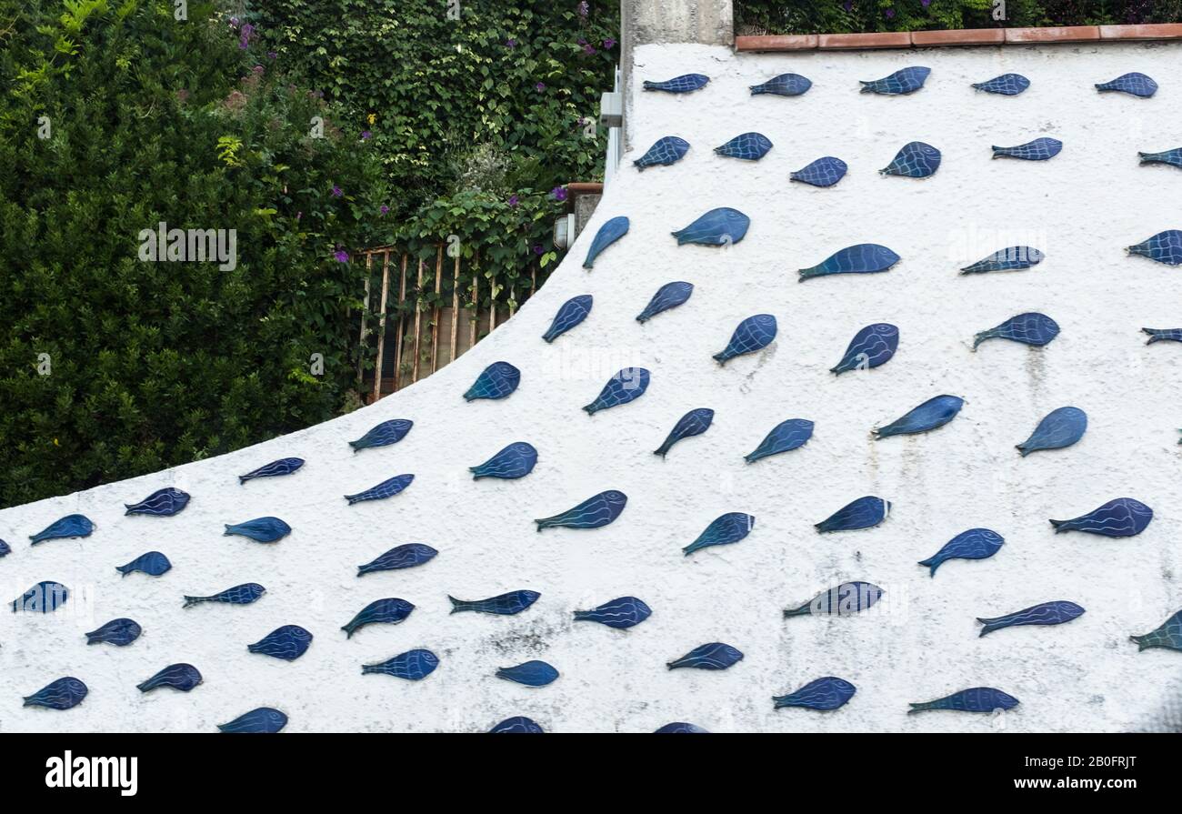 Handmade blue fish tiles decorate a white plaster garden wall on the ...