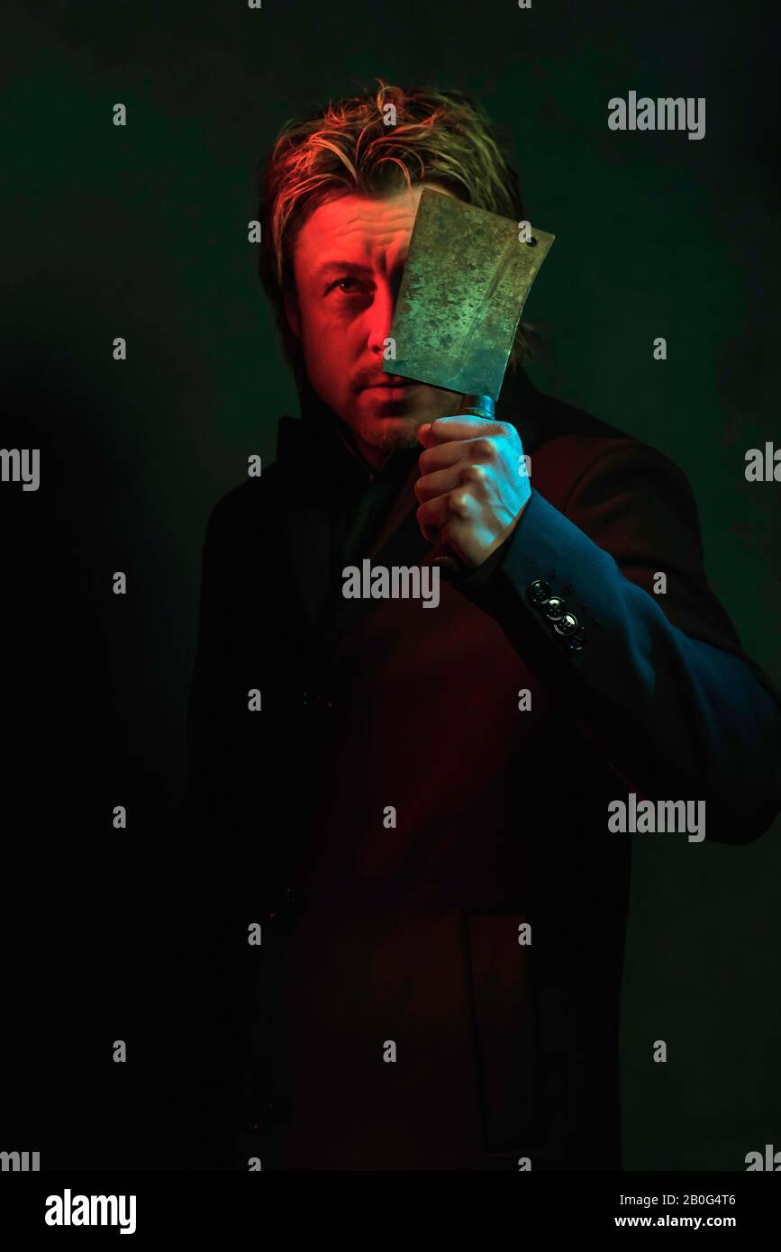 Man holding meat cleaver in front of face. Standing in red and green ...